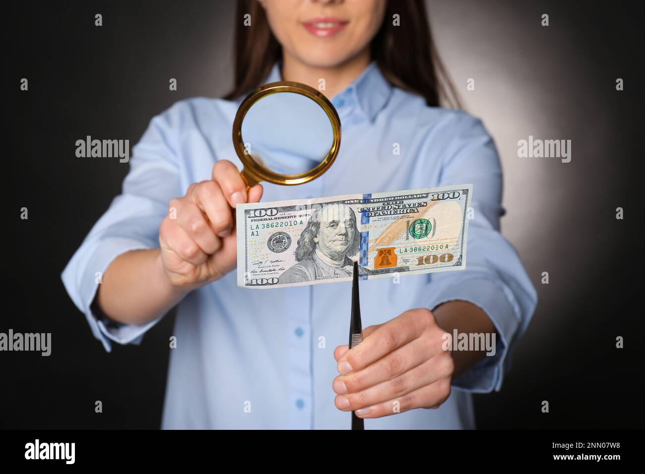 Expert authenticating 100 dollar banknote with magnifying glass against ...