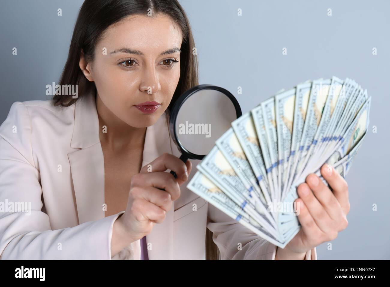 Expert authenticating 100 dollar banknotes with magnifying glass on ...