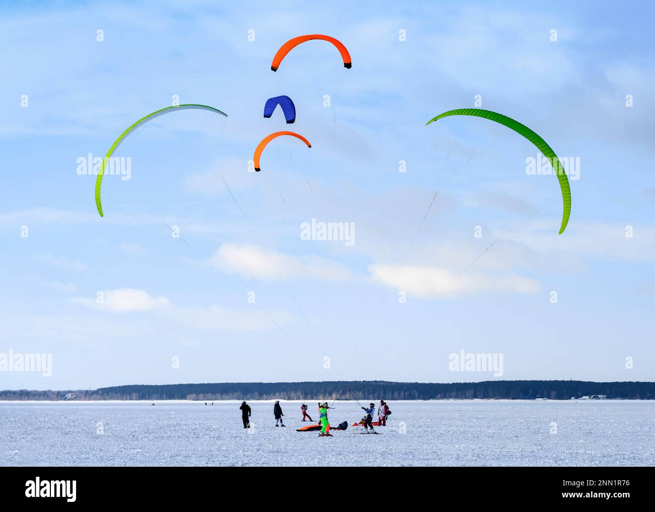 Snowkiting with colored parachutes on a frozen river covered with snow ...