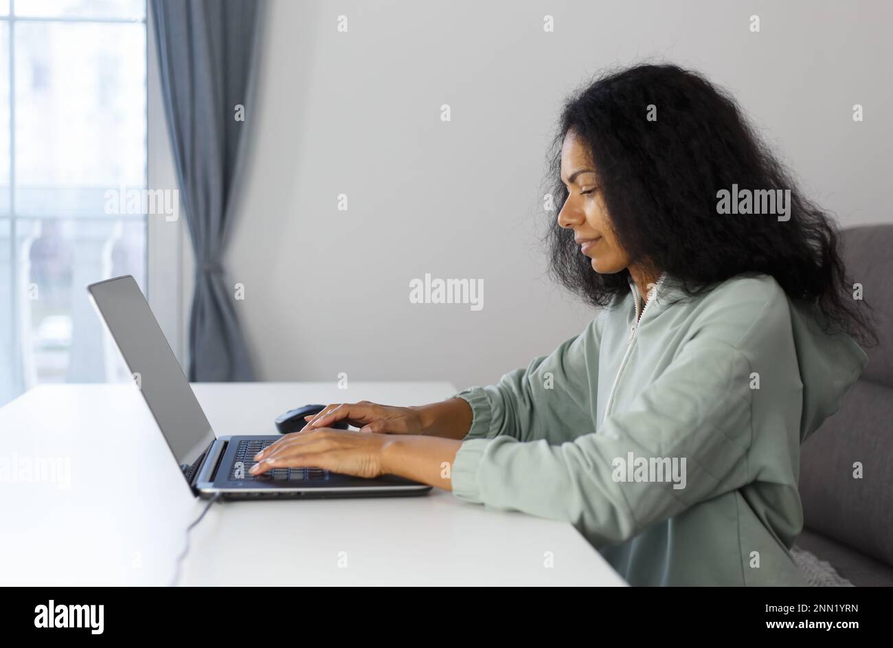 Freelance programmer coding on a laptop at home. Focused black woman ...
