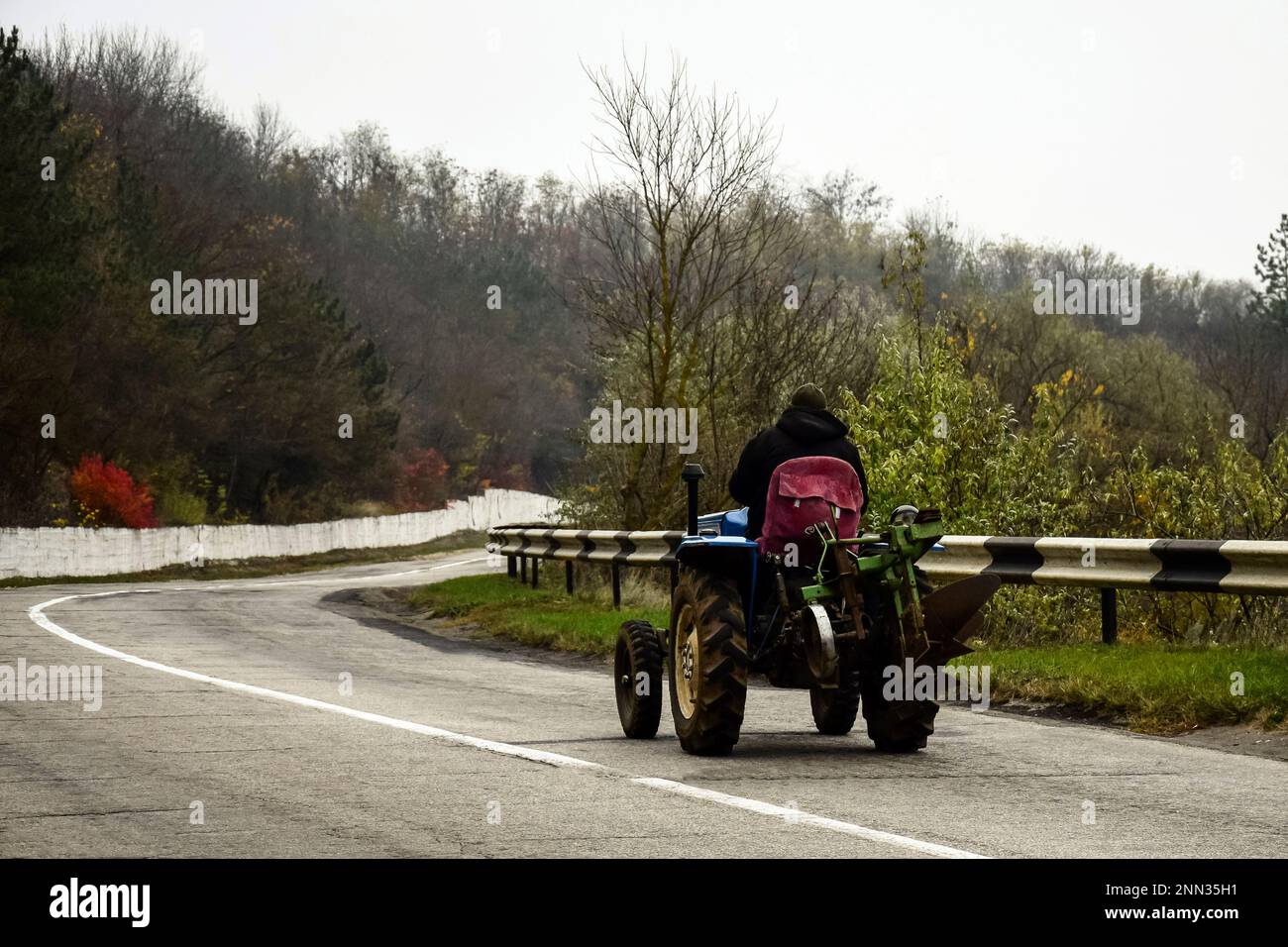 Man on tractor climbs mountain asphalt road. The tractor is equipped ...