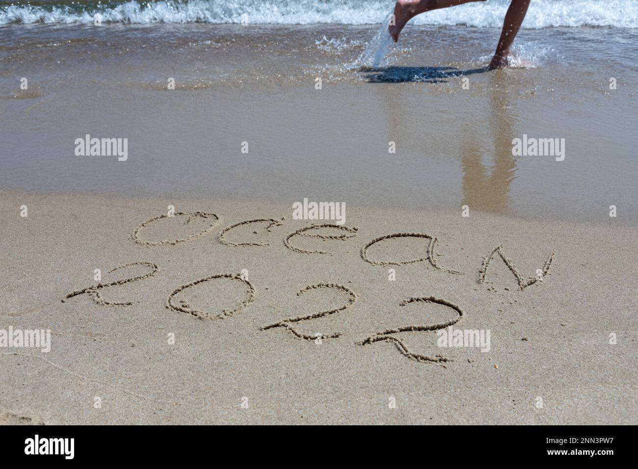 The inscription ocean 2022 on the sand by the water and the rising wave ...