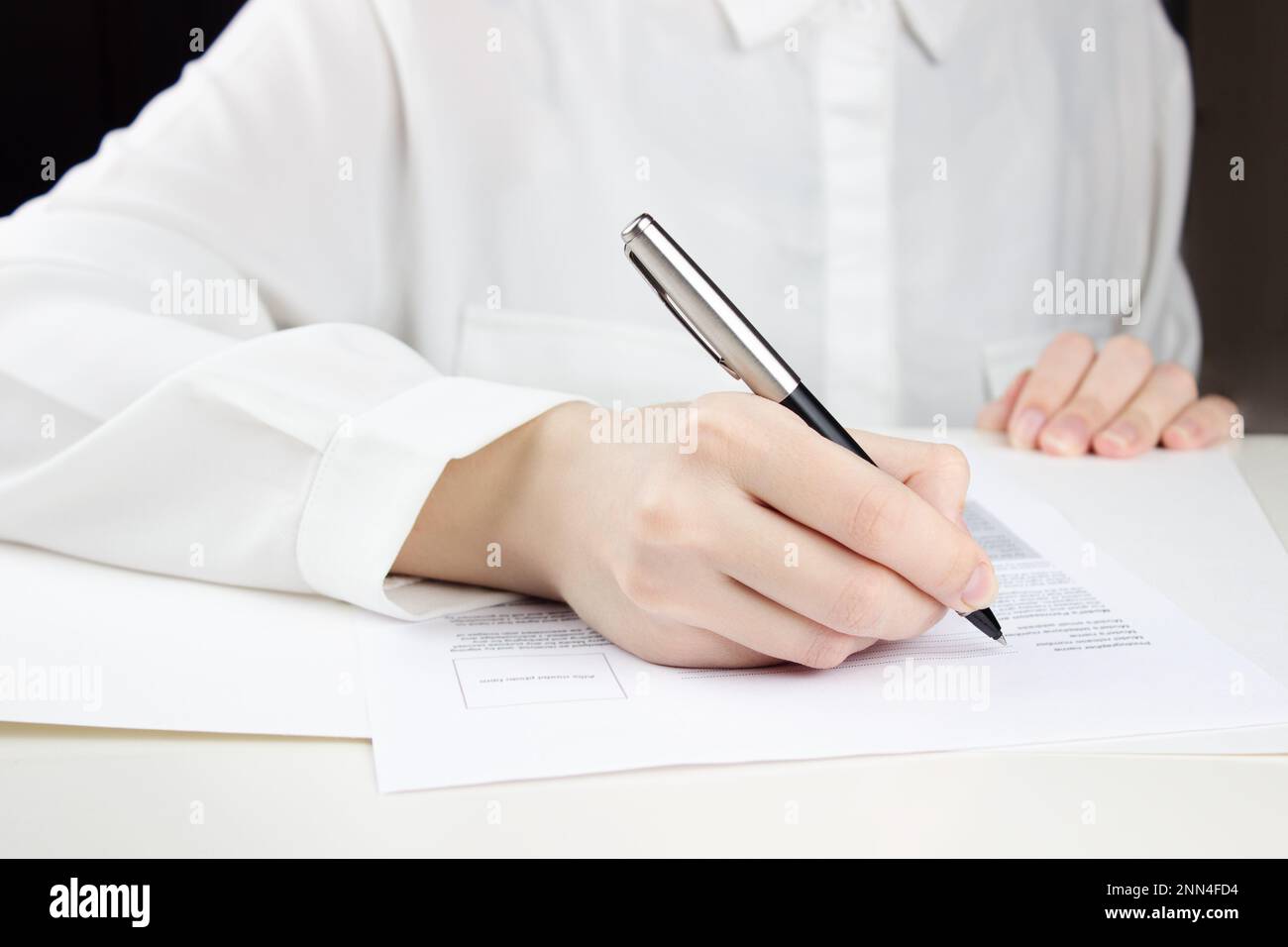 Young woman filling out paperwork signing documents at a high counter ...