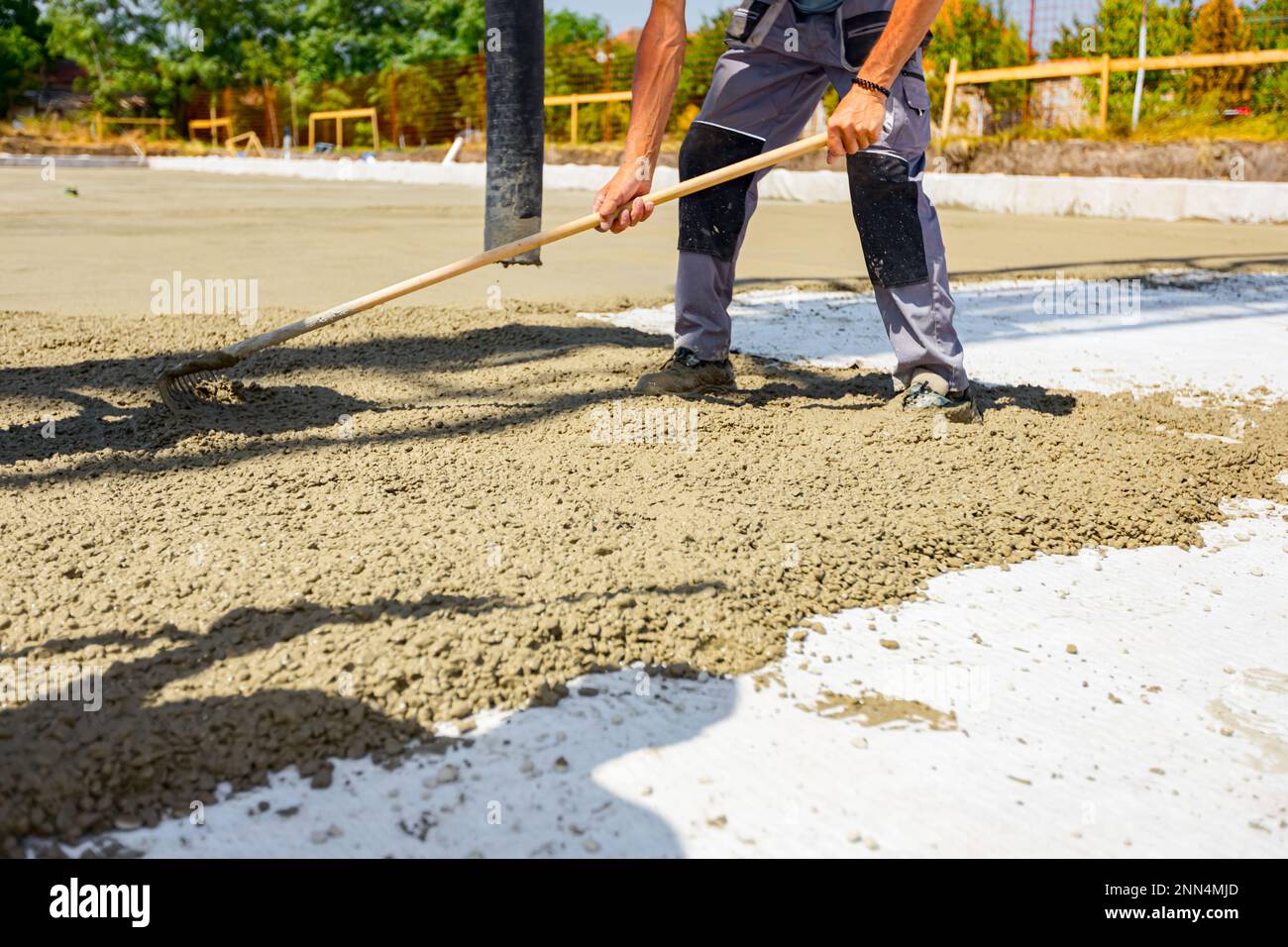 Construction worker, rigger is using rake to spreading, leveling ...