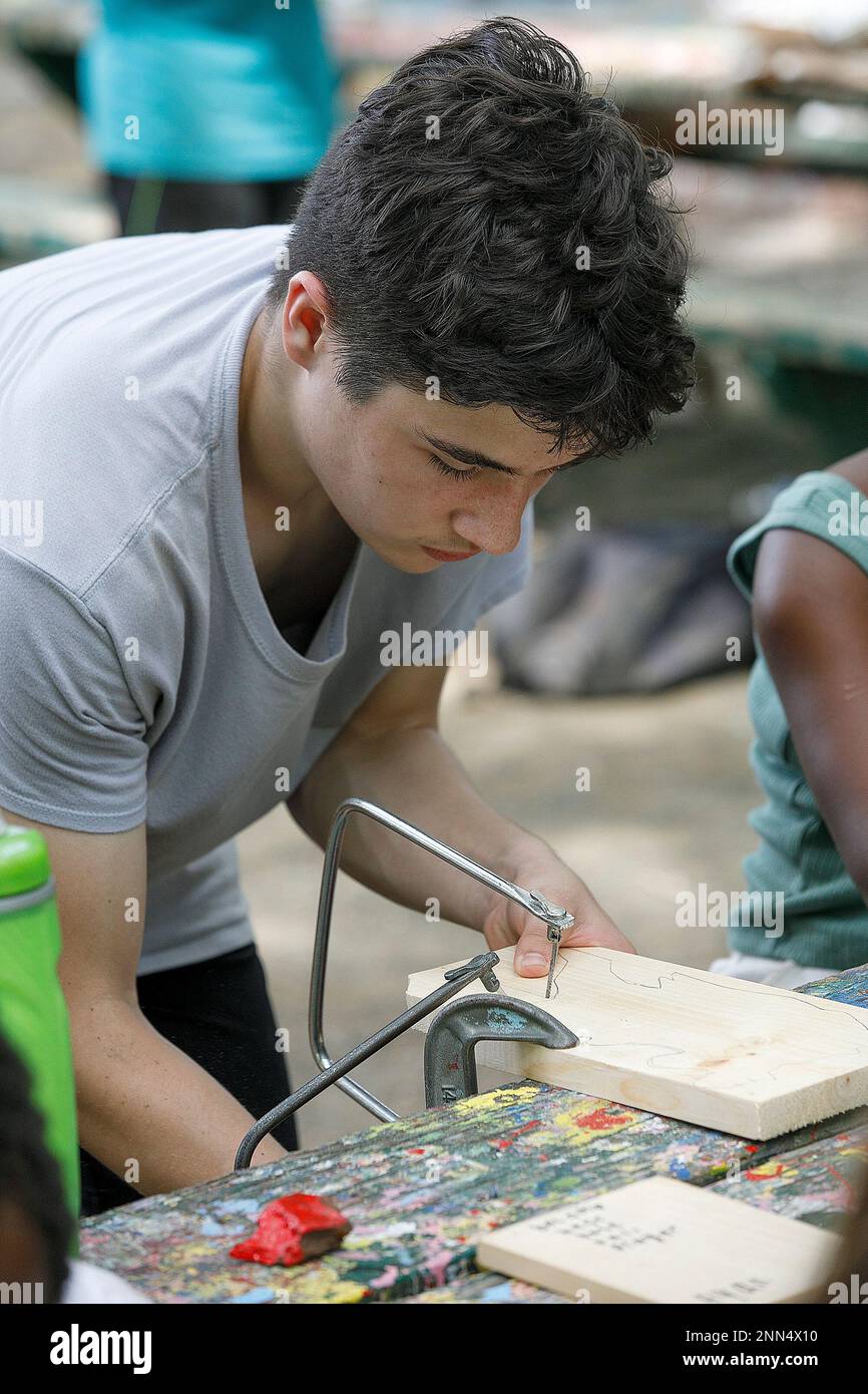 Junior counselor Cameron Osborne, 14, of Meriden, Conn., saws into a wood block while creating a ...