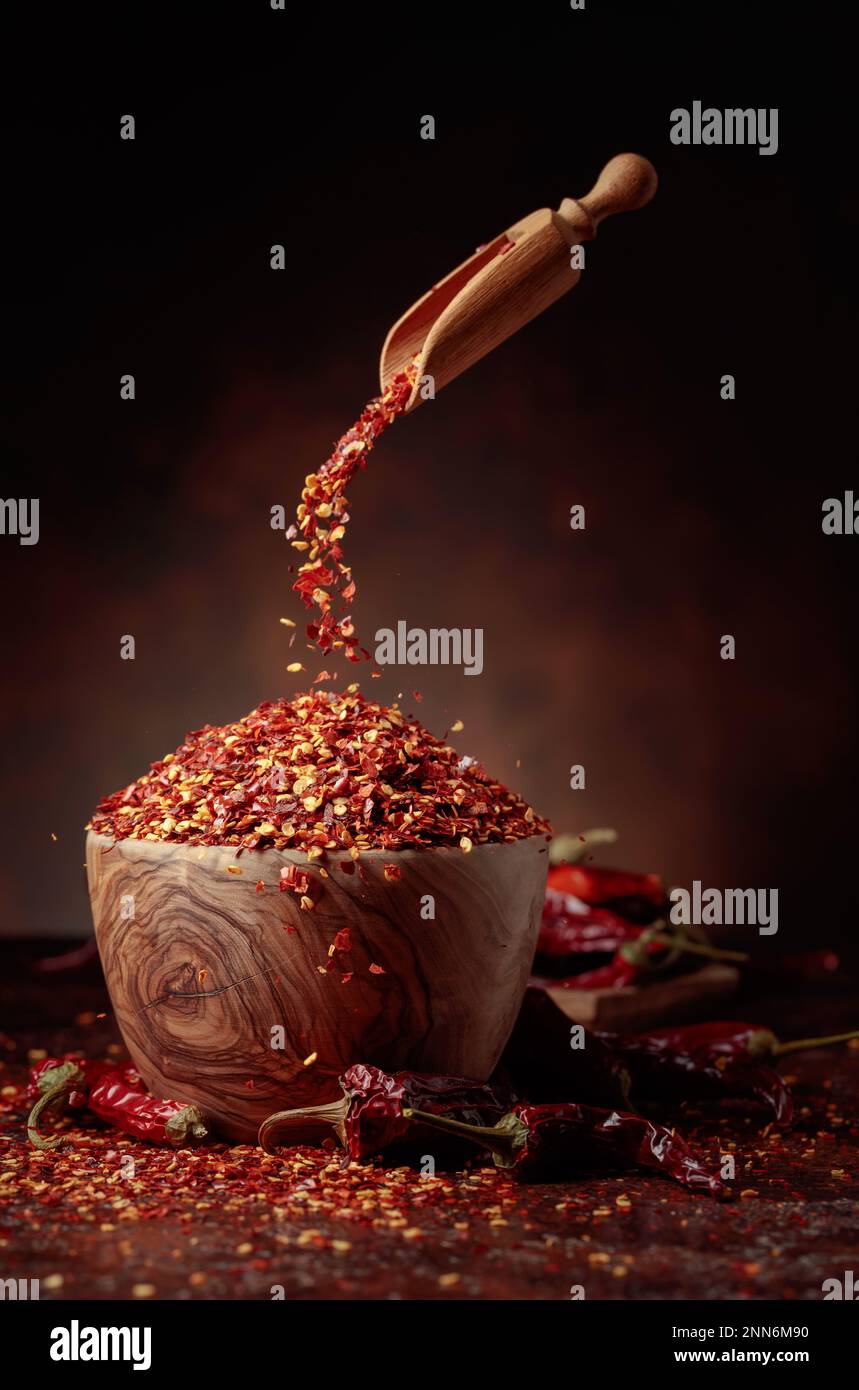 Chilli flakes are poured into a wooden dish. Chilli flakes and dried ...