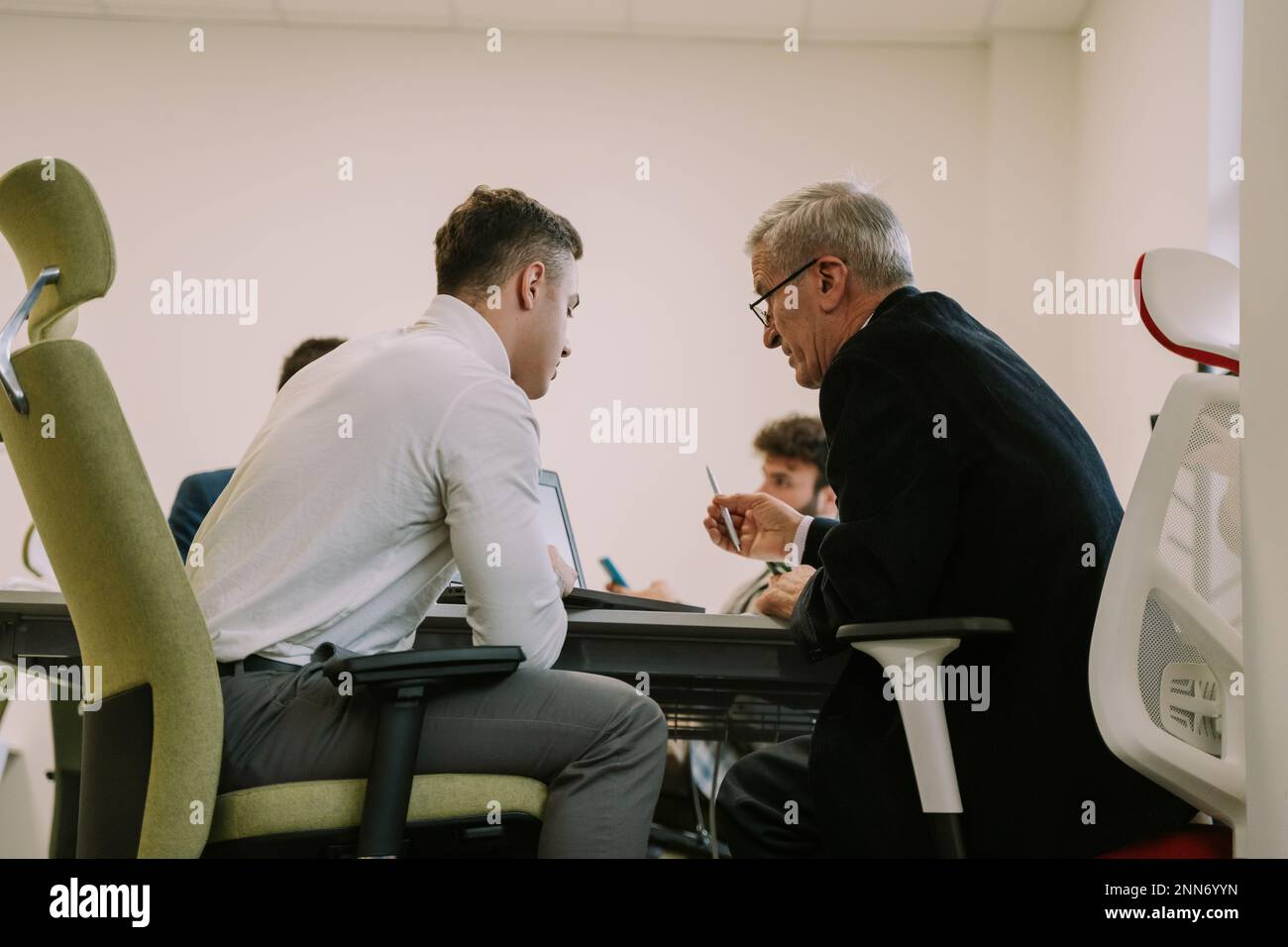 Senior male guiding and tutoring the new young employee at the office ...