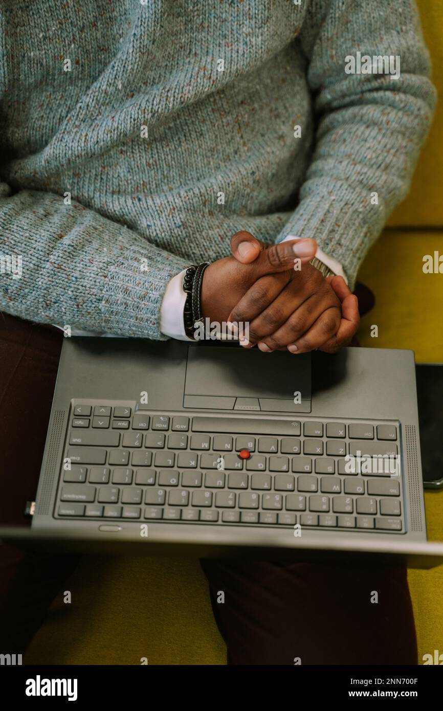 A close up photo of a man with crossed hands and lap top on his lap ...