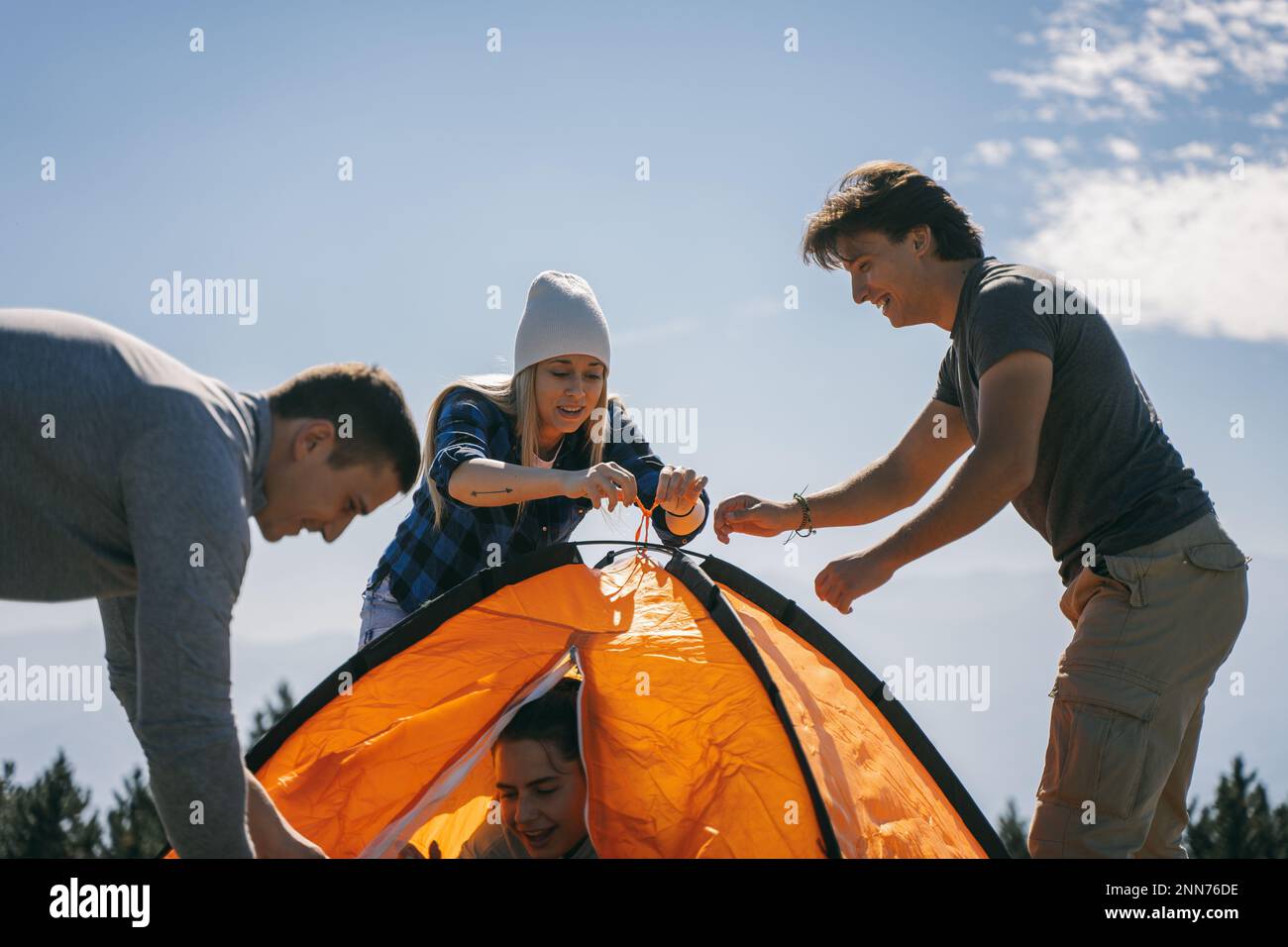 Beautiful blonde girl tieing the knot on the tent with her friends ...