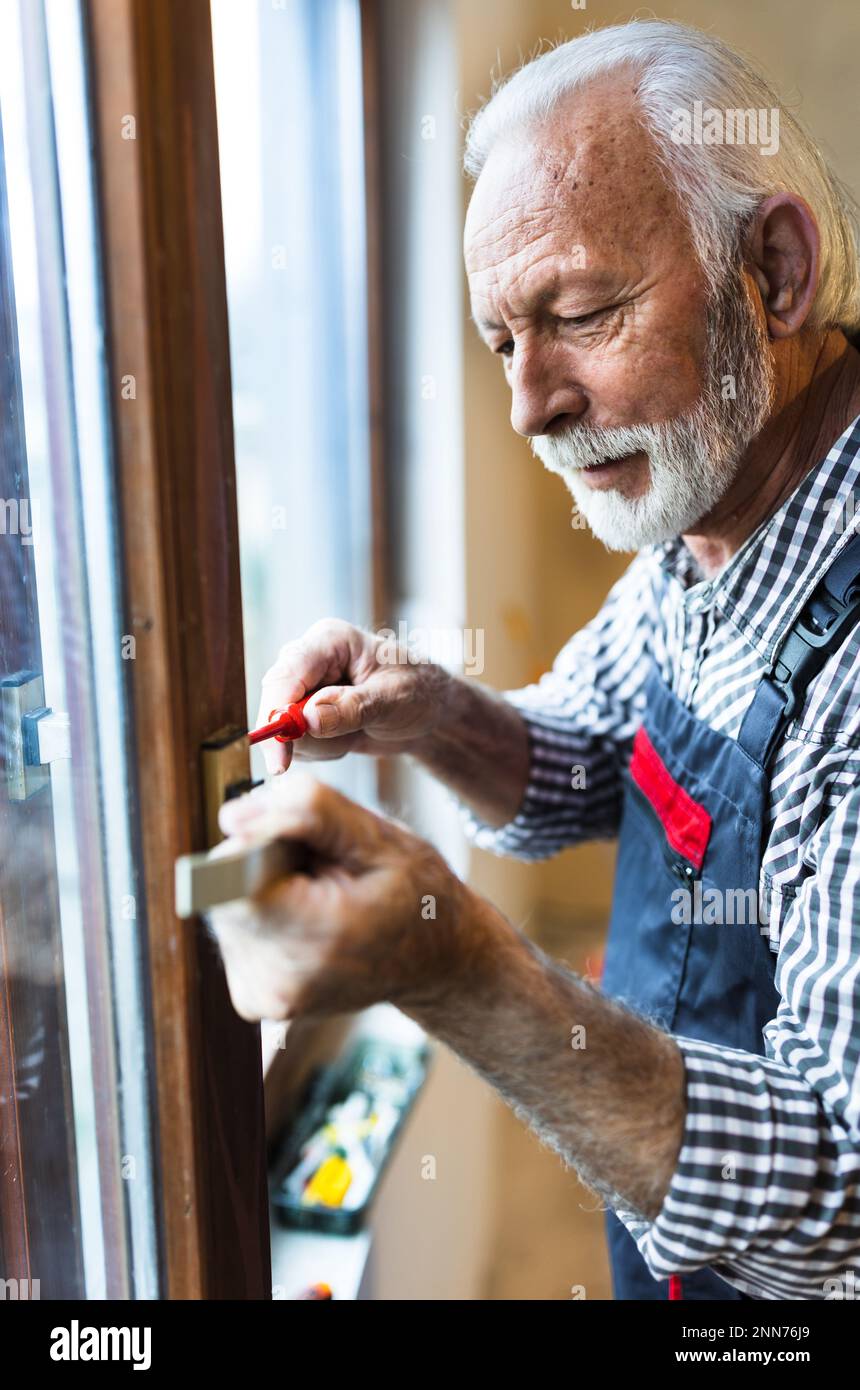 Senior man worker repairing window handle with manual screwdriver in ...