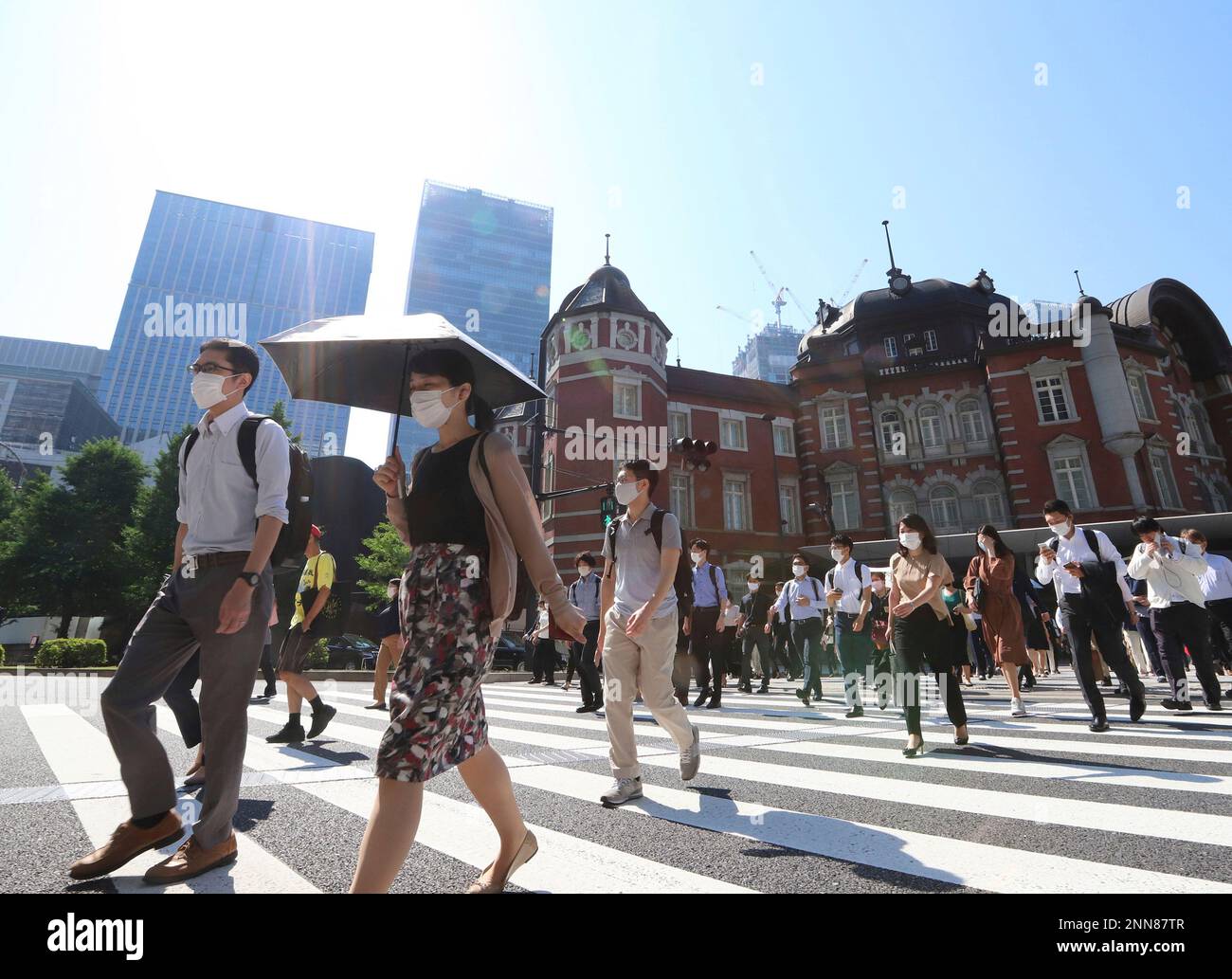 People wearing masks walk in strong sunlight near Tokyo Station in ...