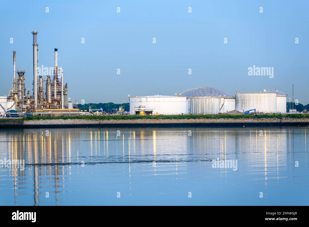 Tanks and distillation towers in a oil refinery on a harbour at dusk ...