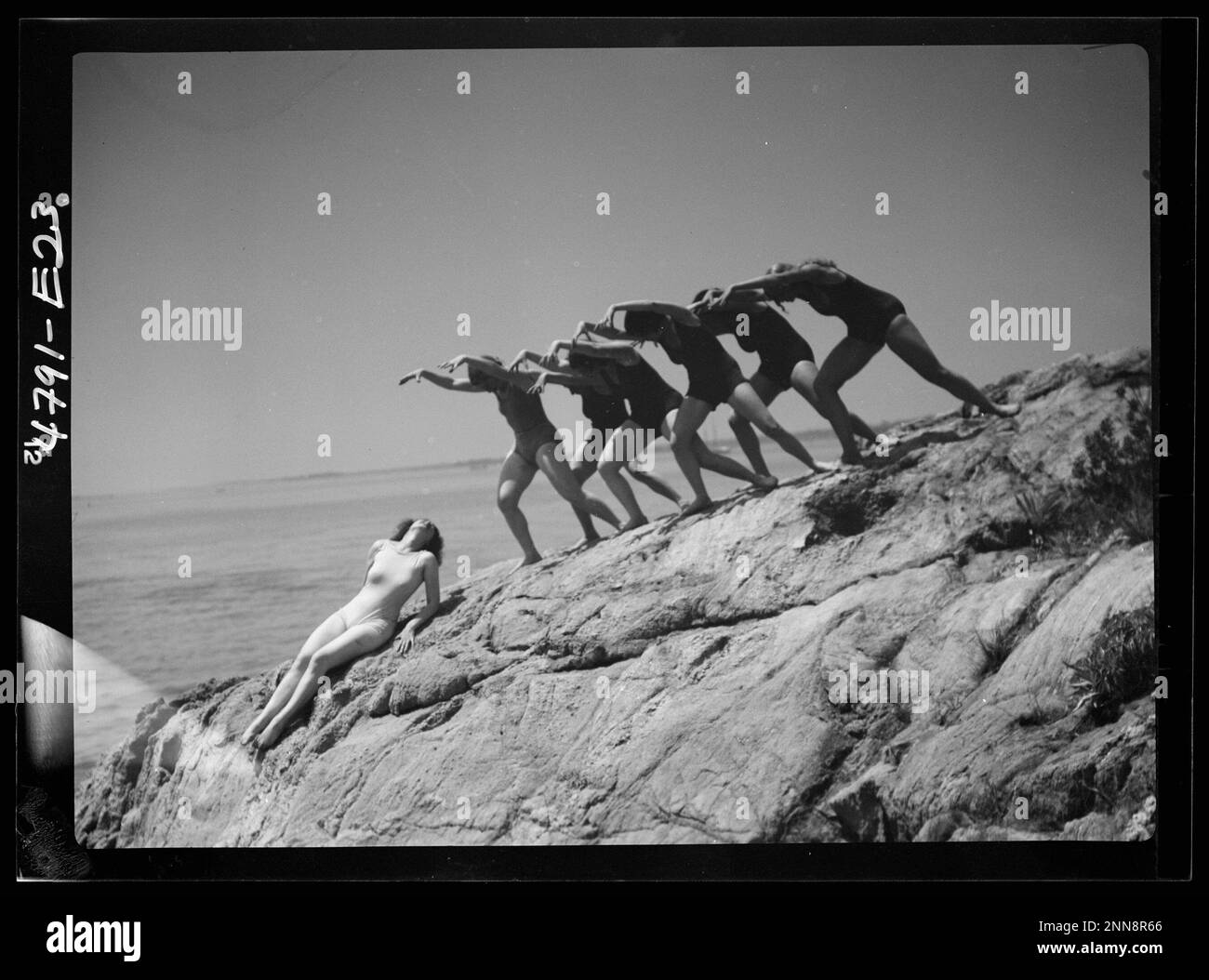 A lone woman lying on a rocky shore is seemingly menaced by six ...