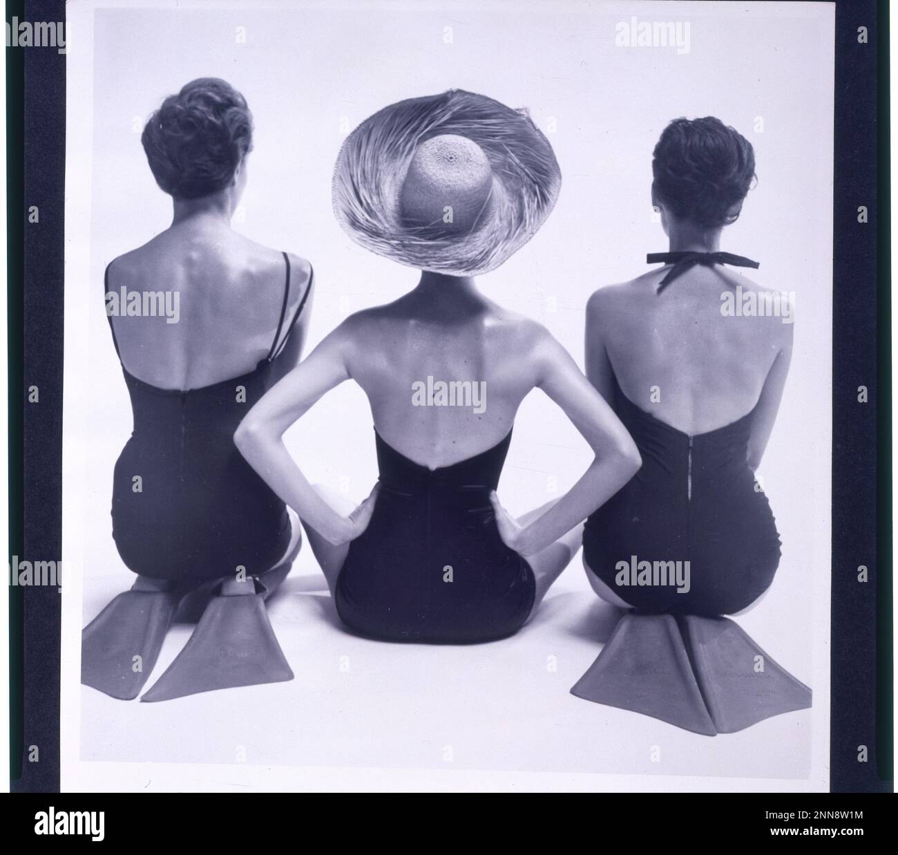 Back view of three female fashion models in swimsuits, two kneeling ...