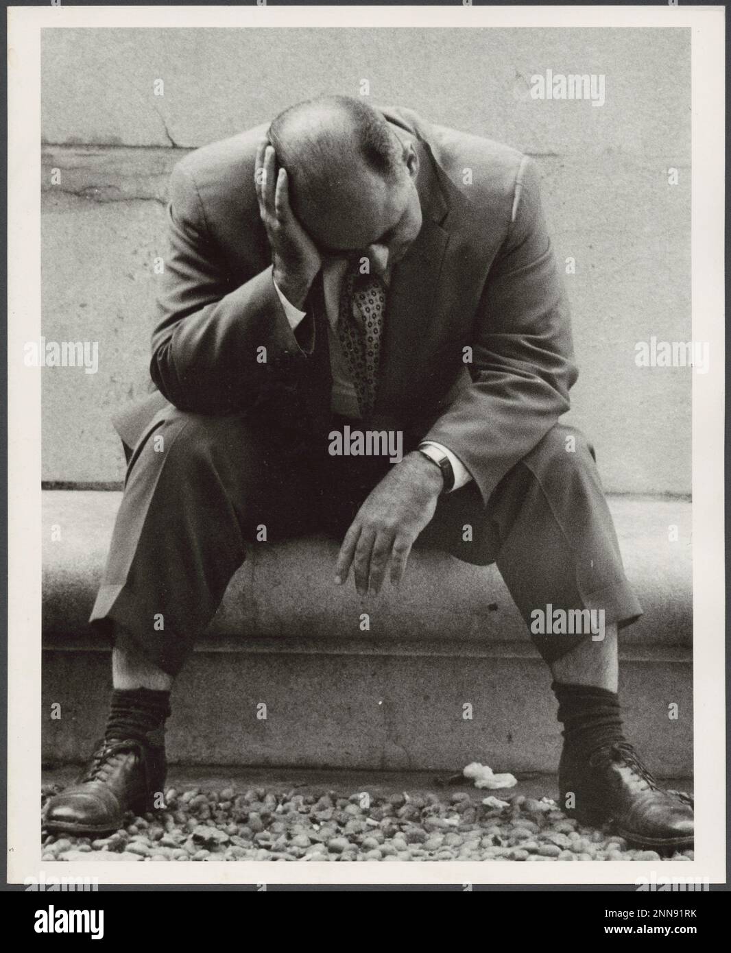 Man sitting on step with head resting on hand, looking at the ground ...