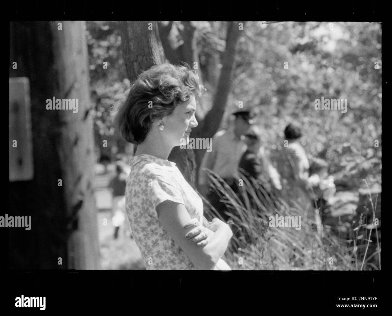 Jacqueline Kennedy, in profile with arms folded, standing outdoors ...