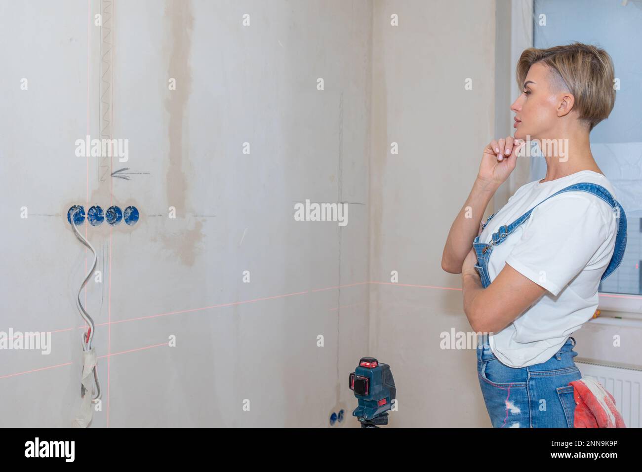 Woman makes repairs in new apartment. Builder levels walls using laser ...