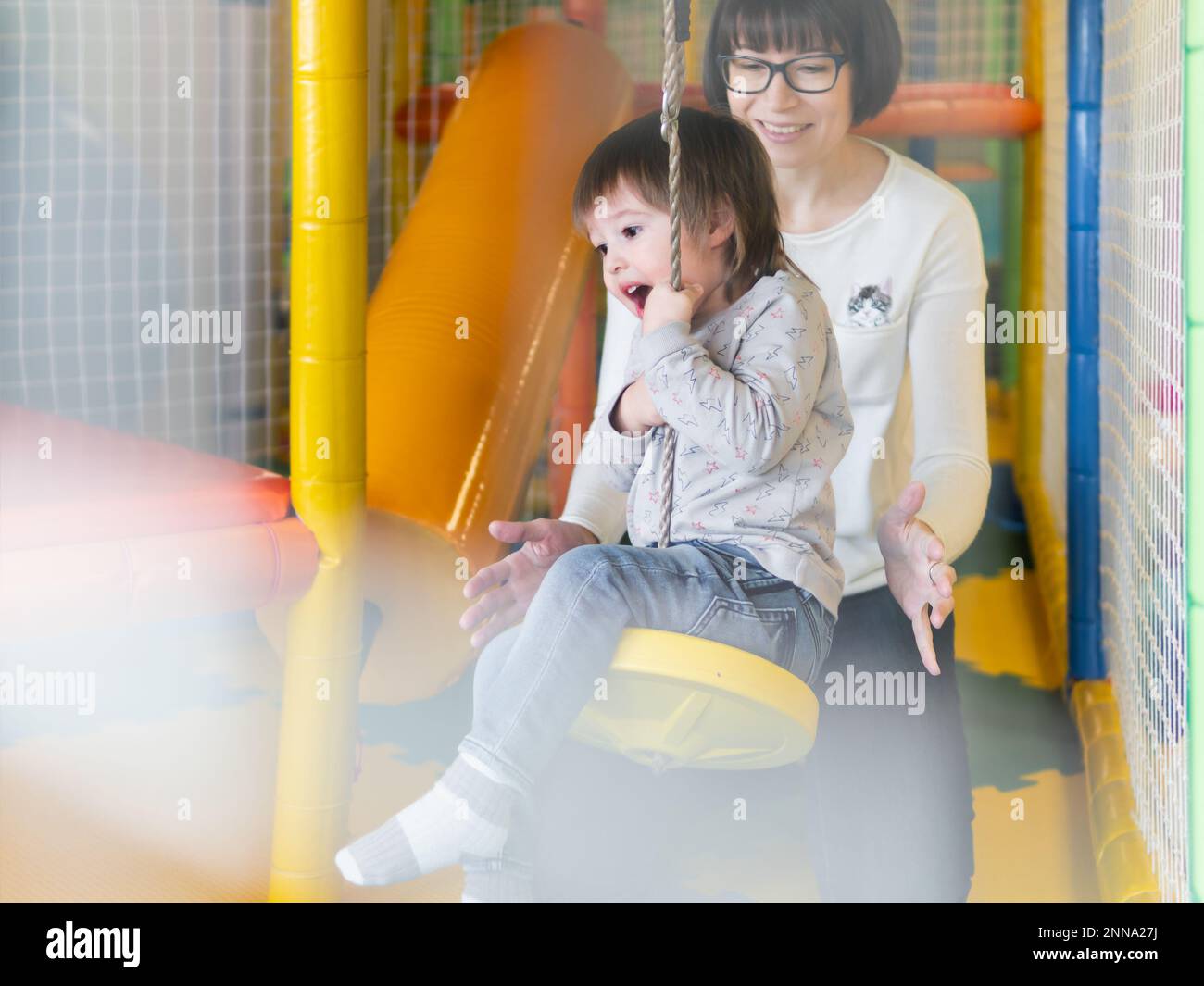 Toddler plays on rope swing with his mother or babysitter. Physical ...