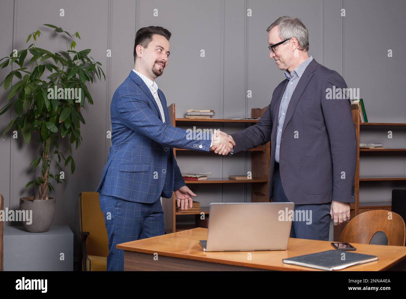 Two business partners in blue suits making handshake in office ...