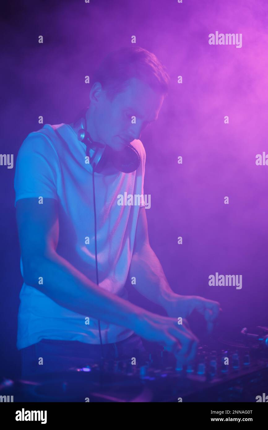 Club DJ plays set in neon lights and smoke. Cool young disc jockey ...