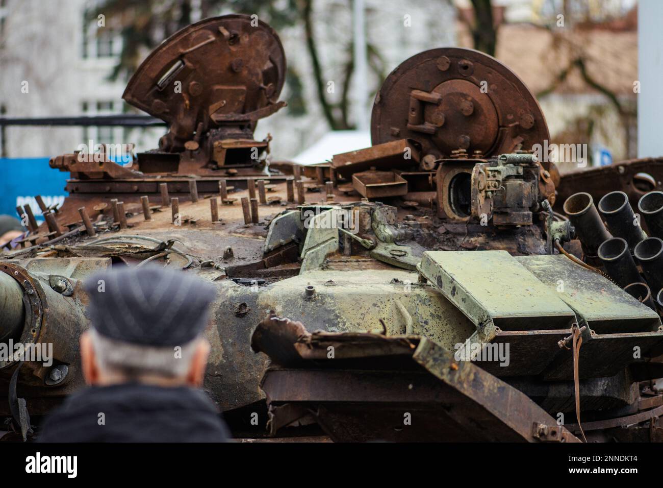 Elderly man looking at a burnt and melted rusty wreckage of a Soviet Russian-made tank T72B ...