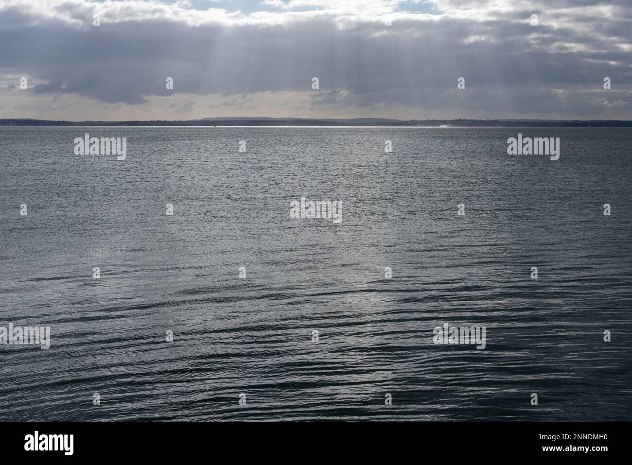 Sun rays breaking through clouds across an empty ocean with land in the ...