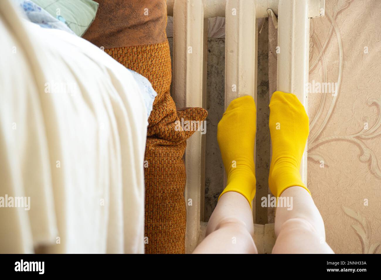 Women's legs in yellow socks are heated on a cast-iron radiator in ...