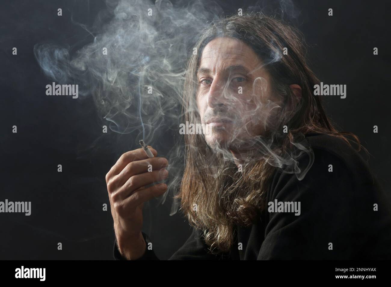 Studio portrait on black background of middle age man with long hair ...