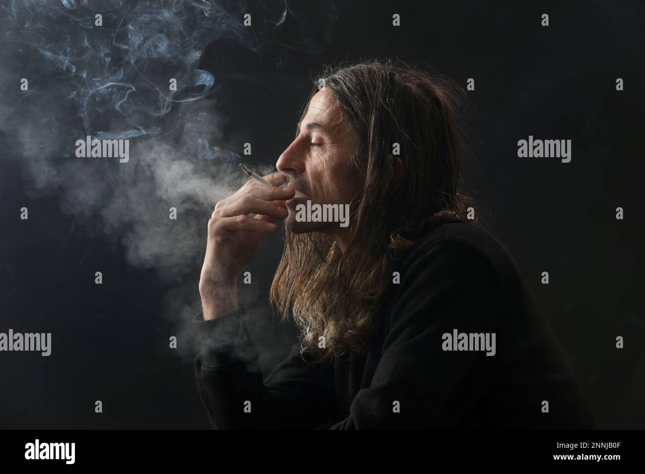 Studio portrait on black background of middle age man with long hair ...