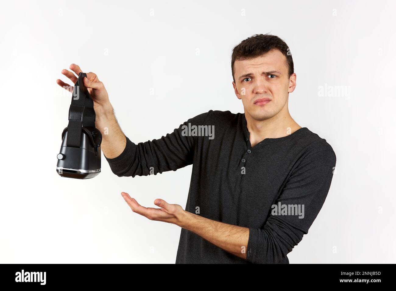 A young man holds a virtual reality helmet in his hands and looks ...