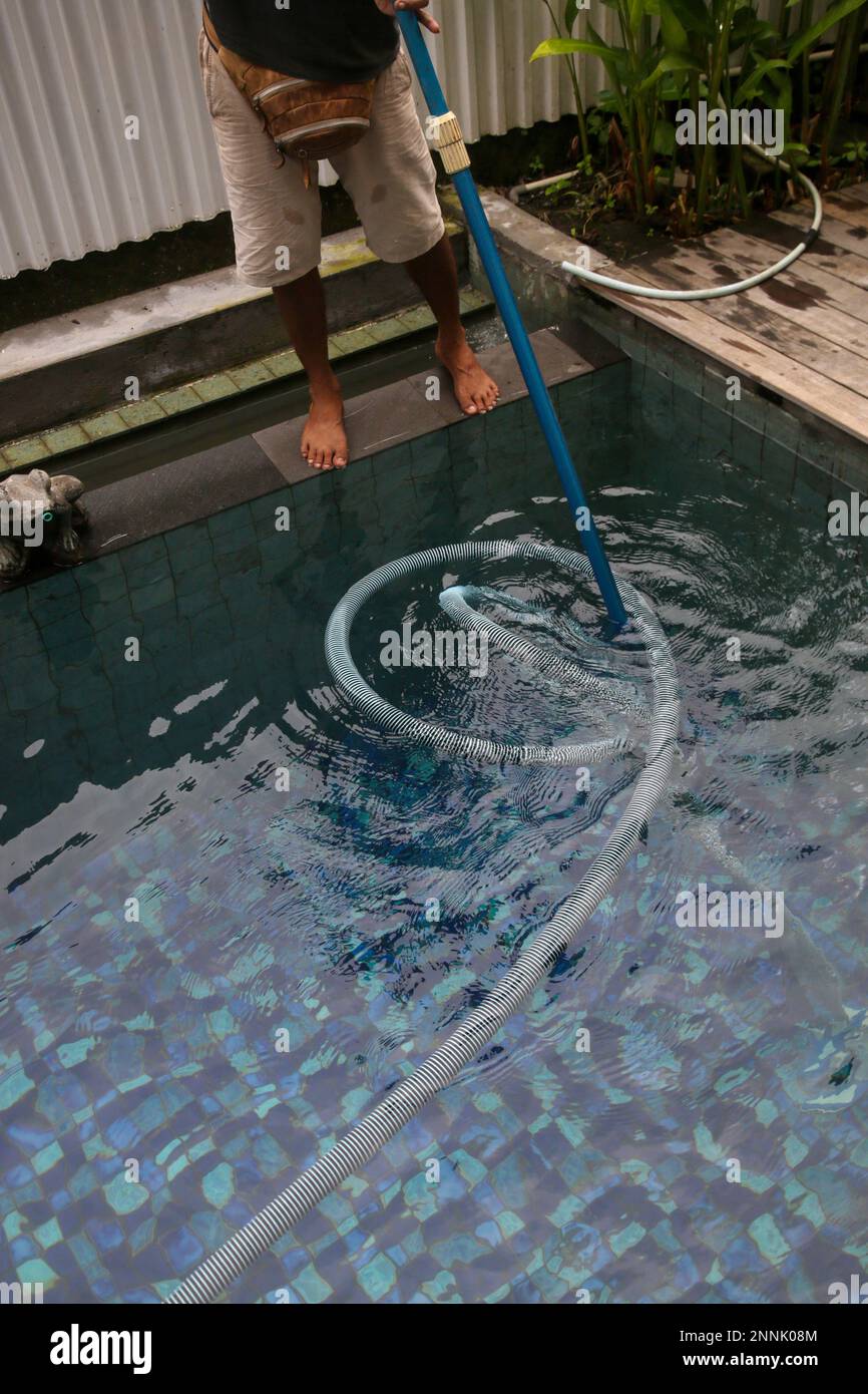 Man cleaning swimming pool with vacuum tube cleaner. Weekly pool ...