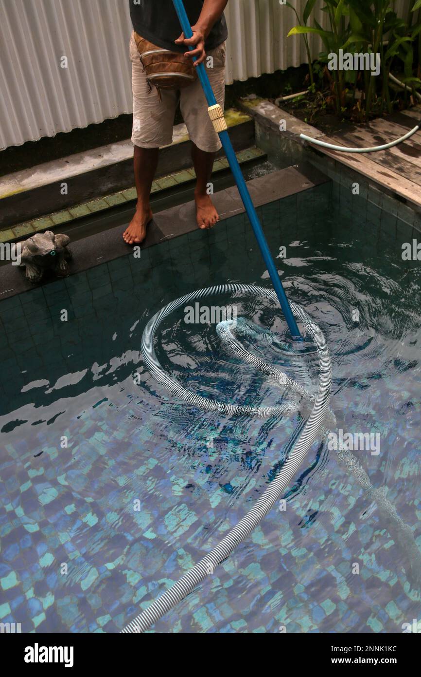 Man cleaning swimming pool with vacuum tube cleaner. Weekly pool ...
