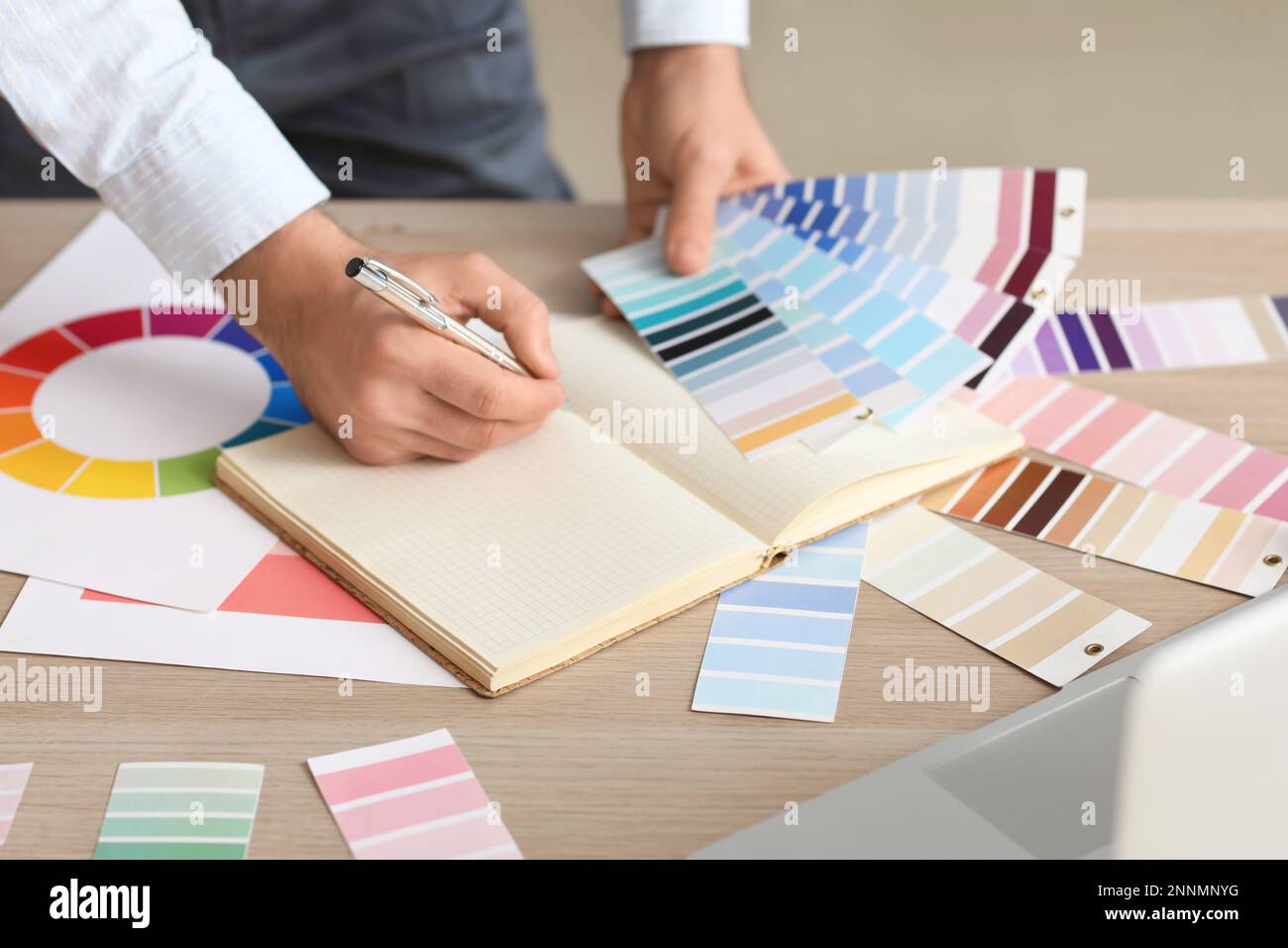 Male painter with color palettes writing in notebook at table, closeup ...