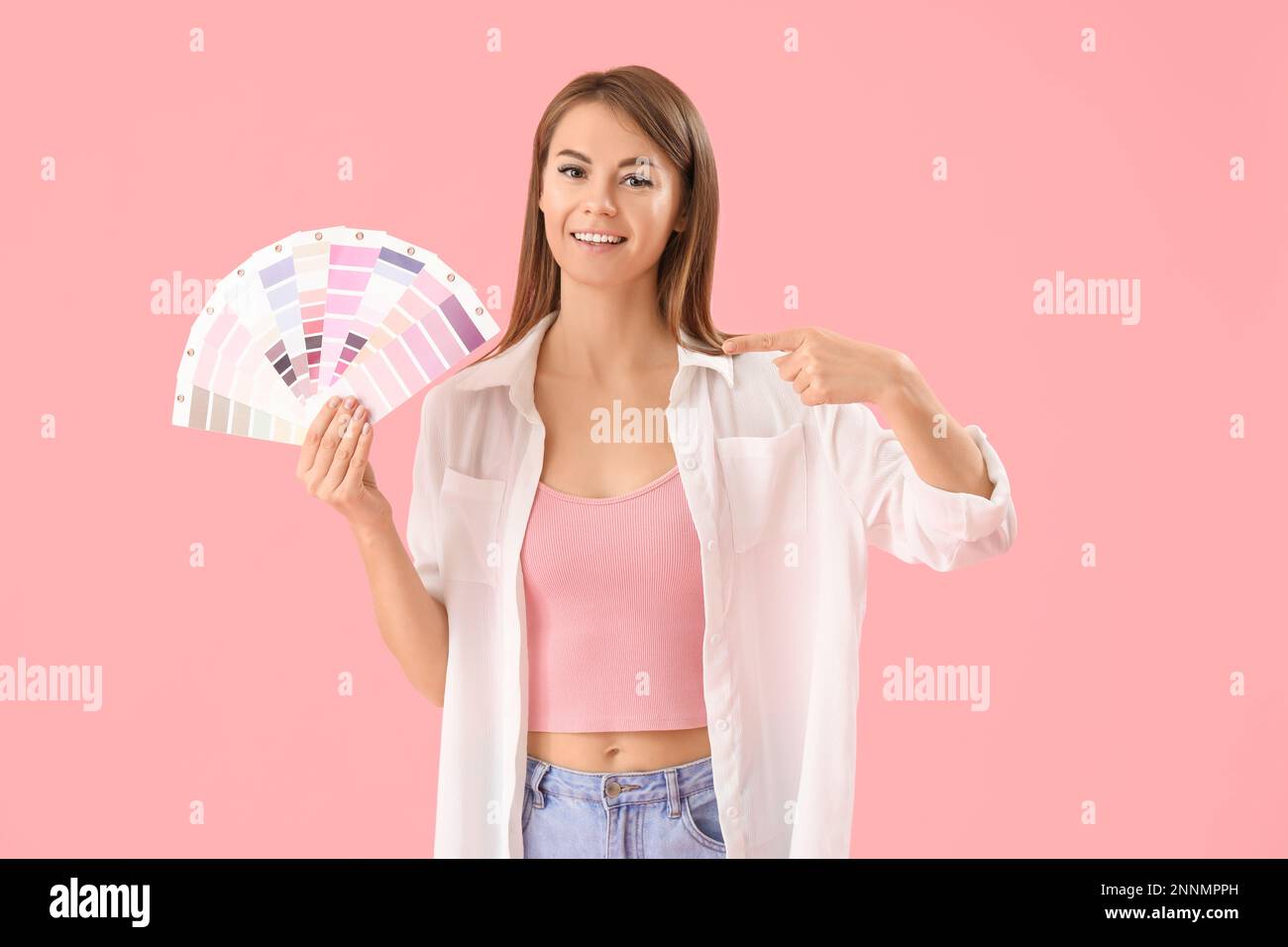 Beautiful woman pointing at paint color palettes on pink background ...