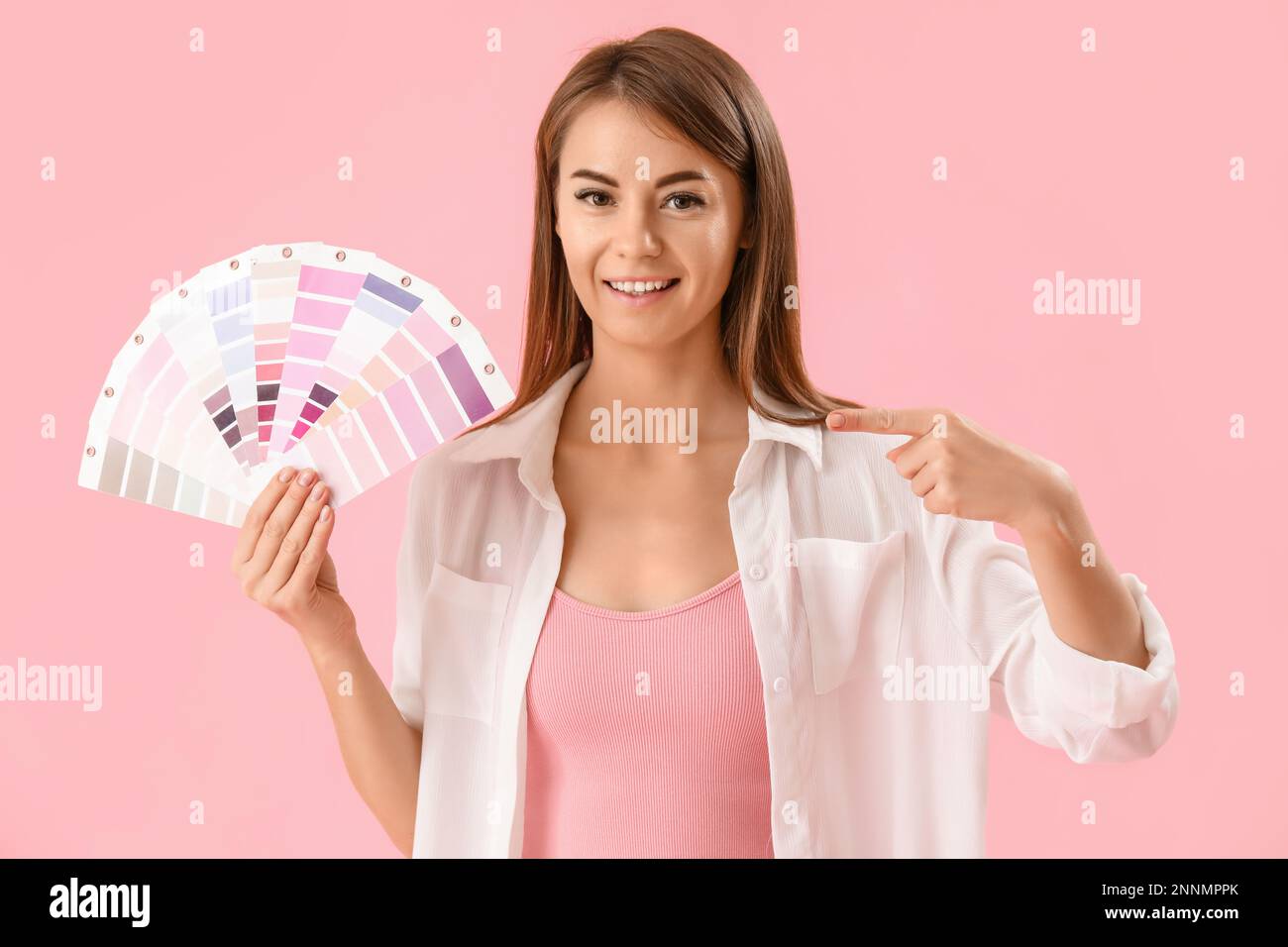 Beautiful woman pointing at paint color palettes on pink background ...