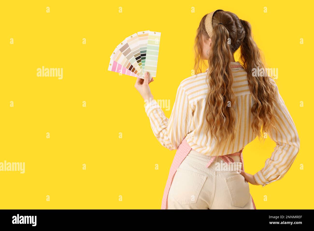 Female artist with paint color palettes on yellow background, back view ...