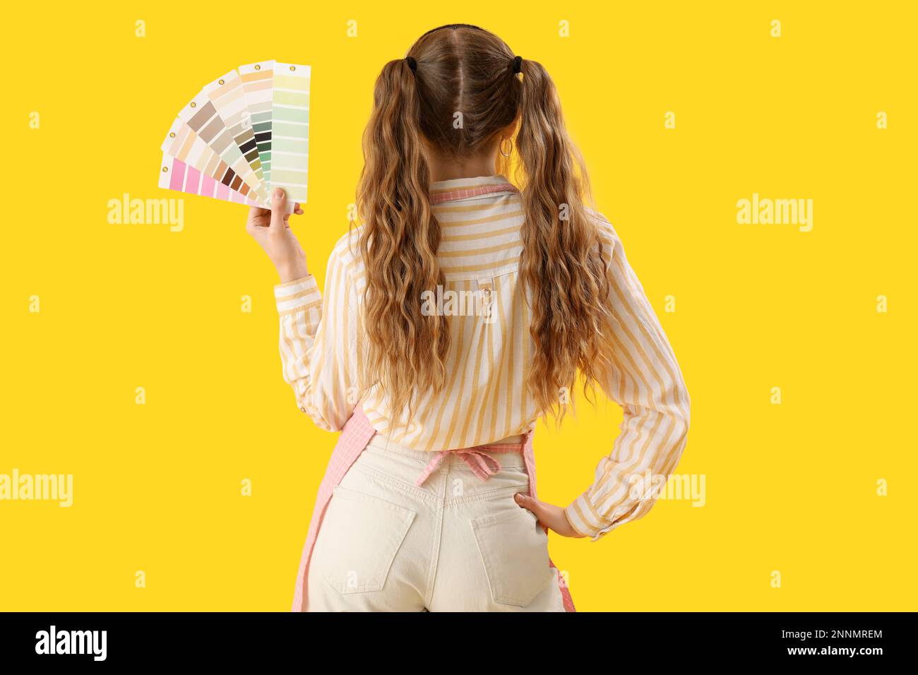 Female artist with paint color palettes on yellow background, back view ...