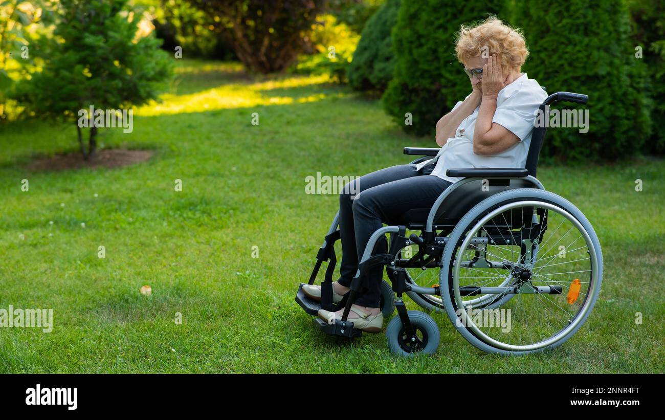 Unhappy elderly woman crying while sitting in a wheelchair on a walk ...