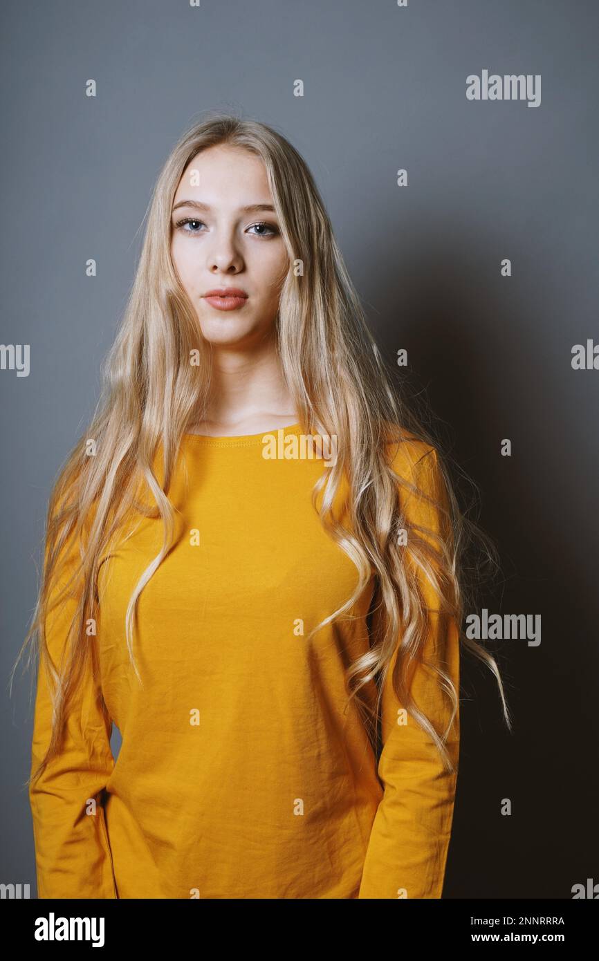 serene teenage girl with very long blond hair against gray background ...