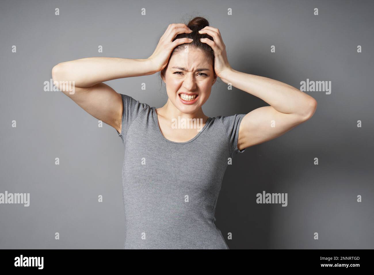 stressed young woman in despair or pain with hands holding head - gray ...
