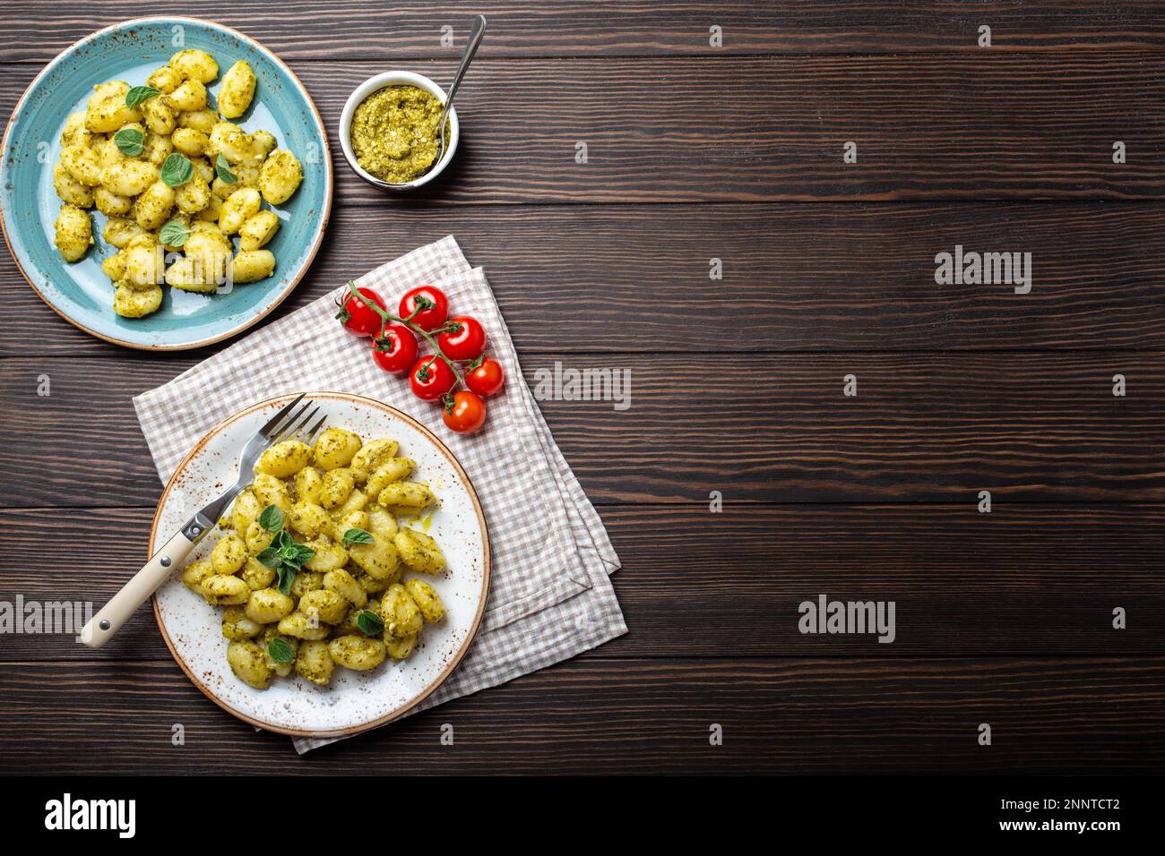 Gnocchi in plates with green pesto sauce, tomatoes and herbs on rustic ...