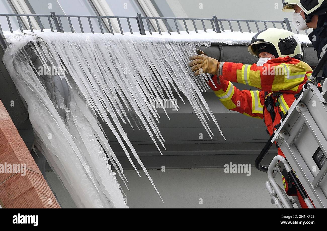 Firefighters break large icicles from the gutter of a house in the city ...