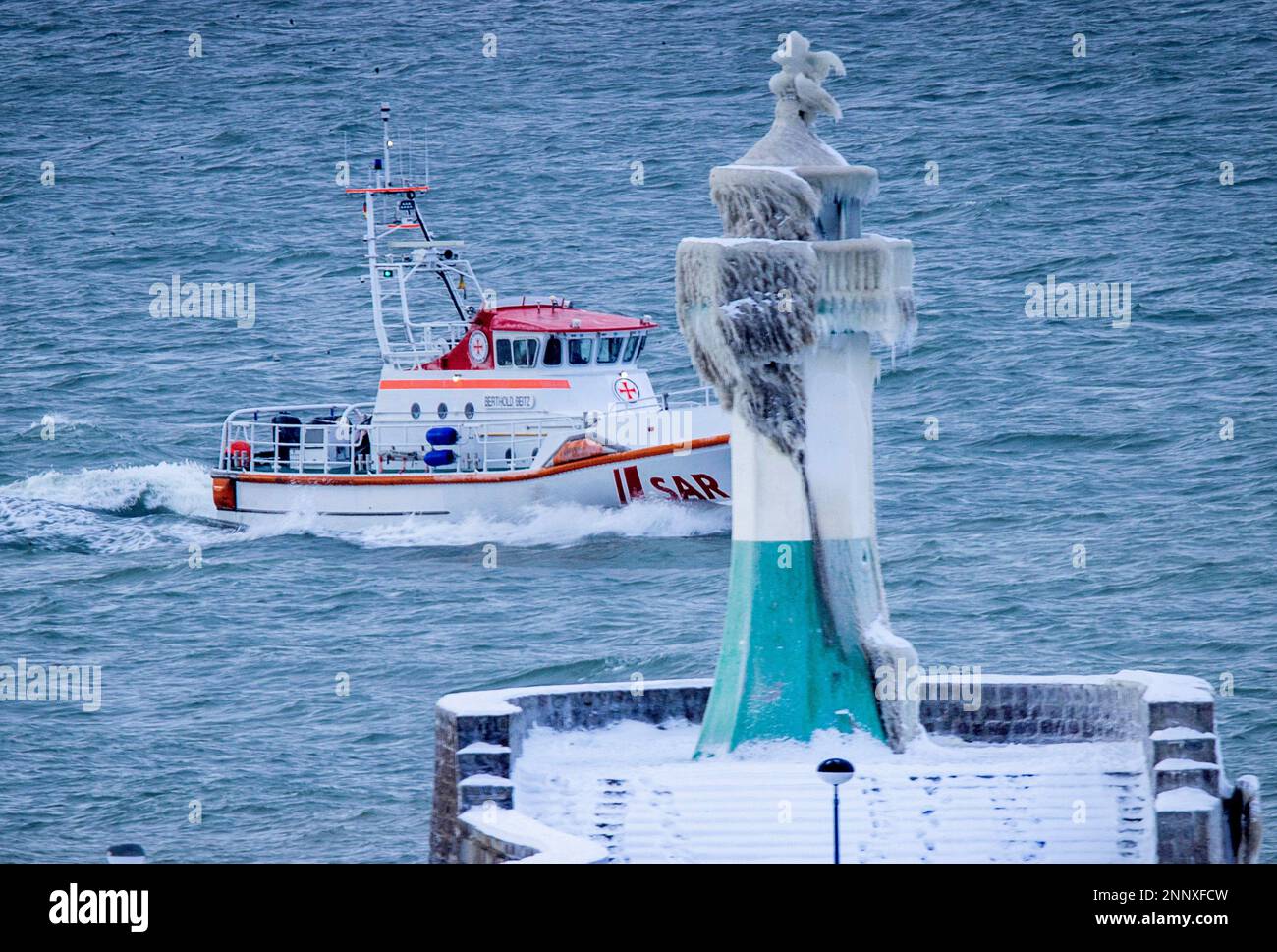 The lifeboat of the sea rescuers passes the icy lighthouse on the ...