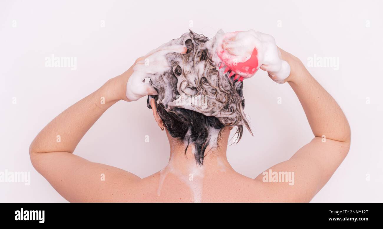 Lady with foam in her hair takes care of her scalp with pink massager ...