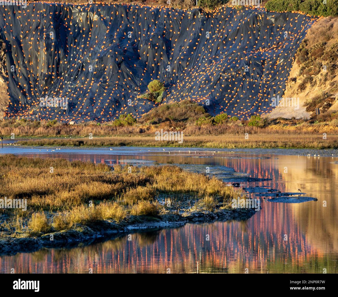 A sandbagged hillside in Newport Beach's Back Bay reflects on water on ...