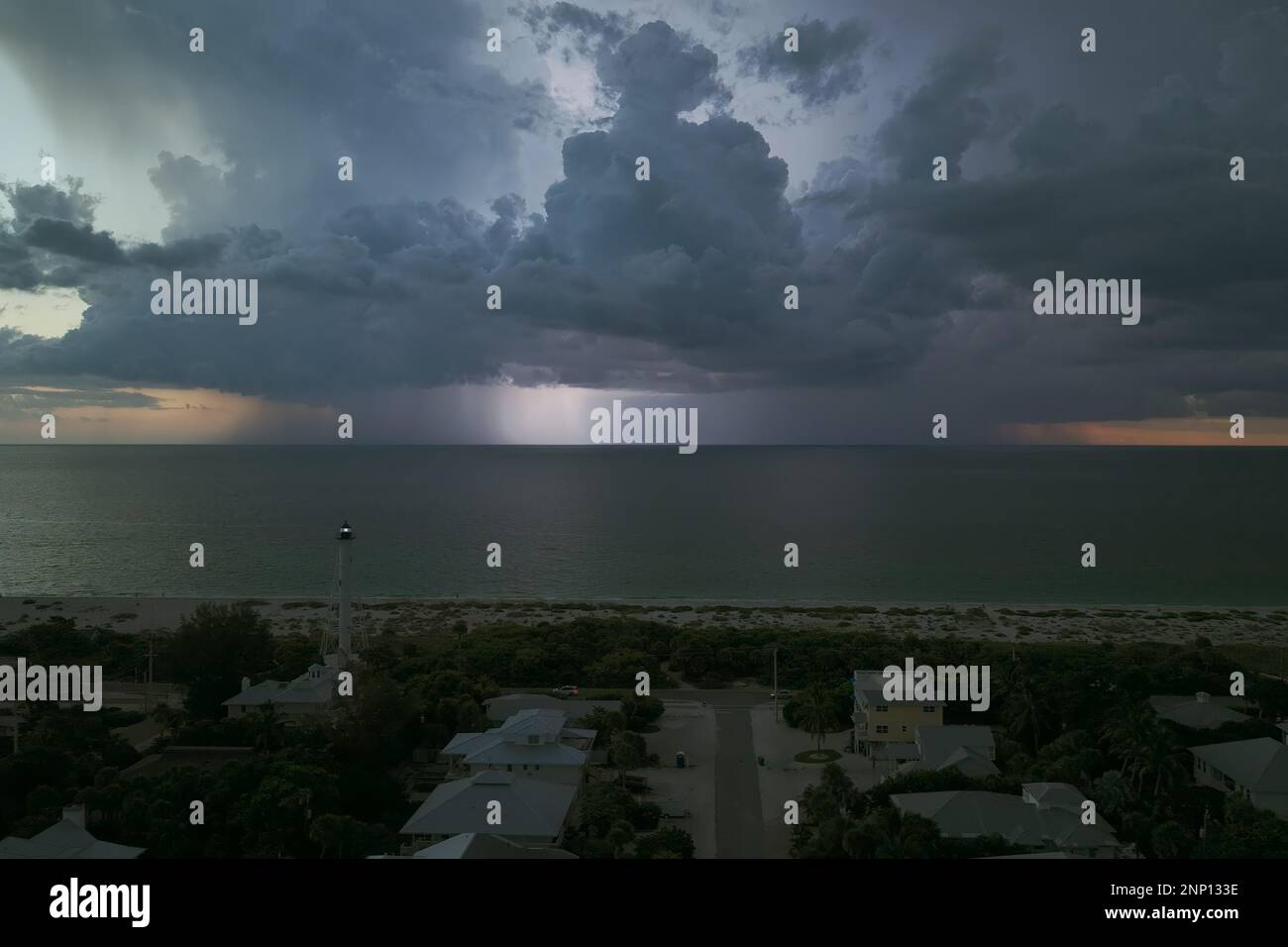 Seashore town with dark houses and tall lighthouse on ocean shore with ...