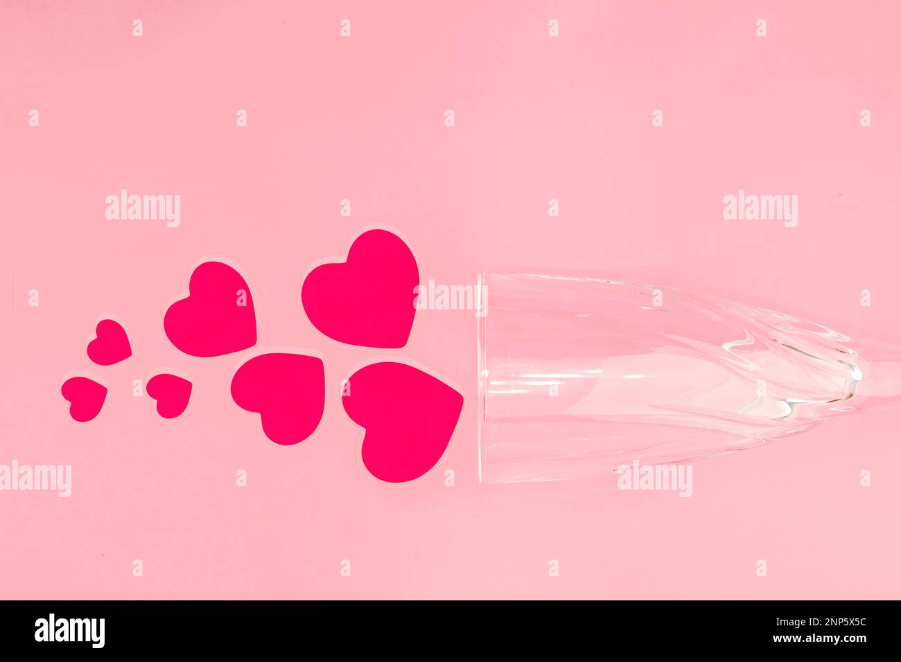 Pink hearts fall out of a glass goblet that lies on a pink background ...