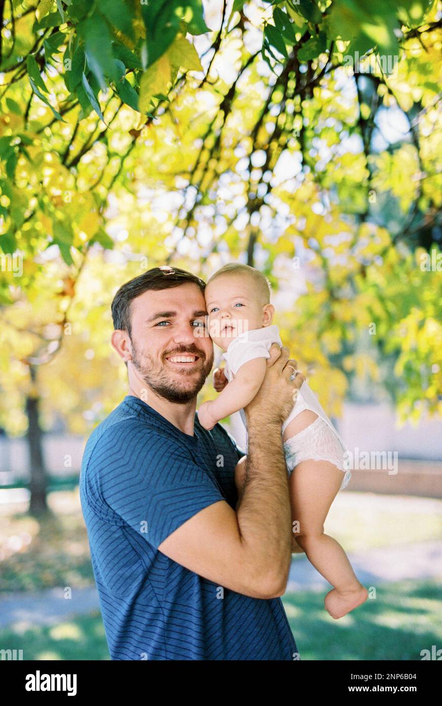 Dad holding a baby in a diaper in his arms standing under a tree Stock ...