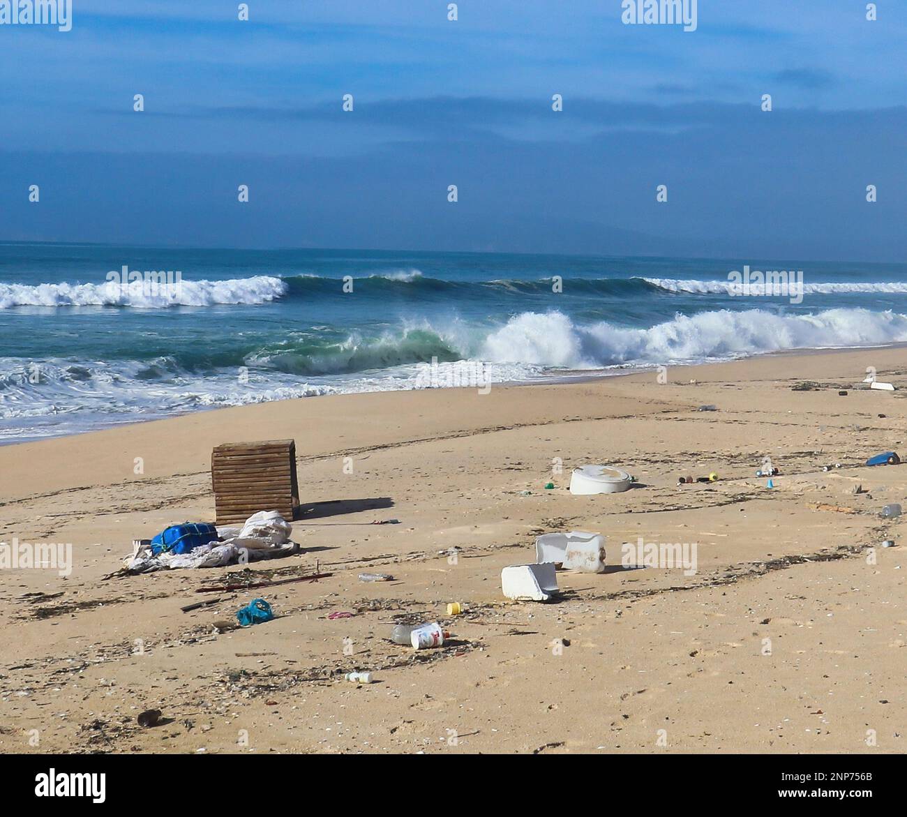 Garbage on a beach with waves crashing in the ocean on a warm winter ...