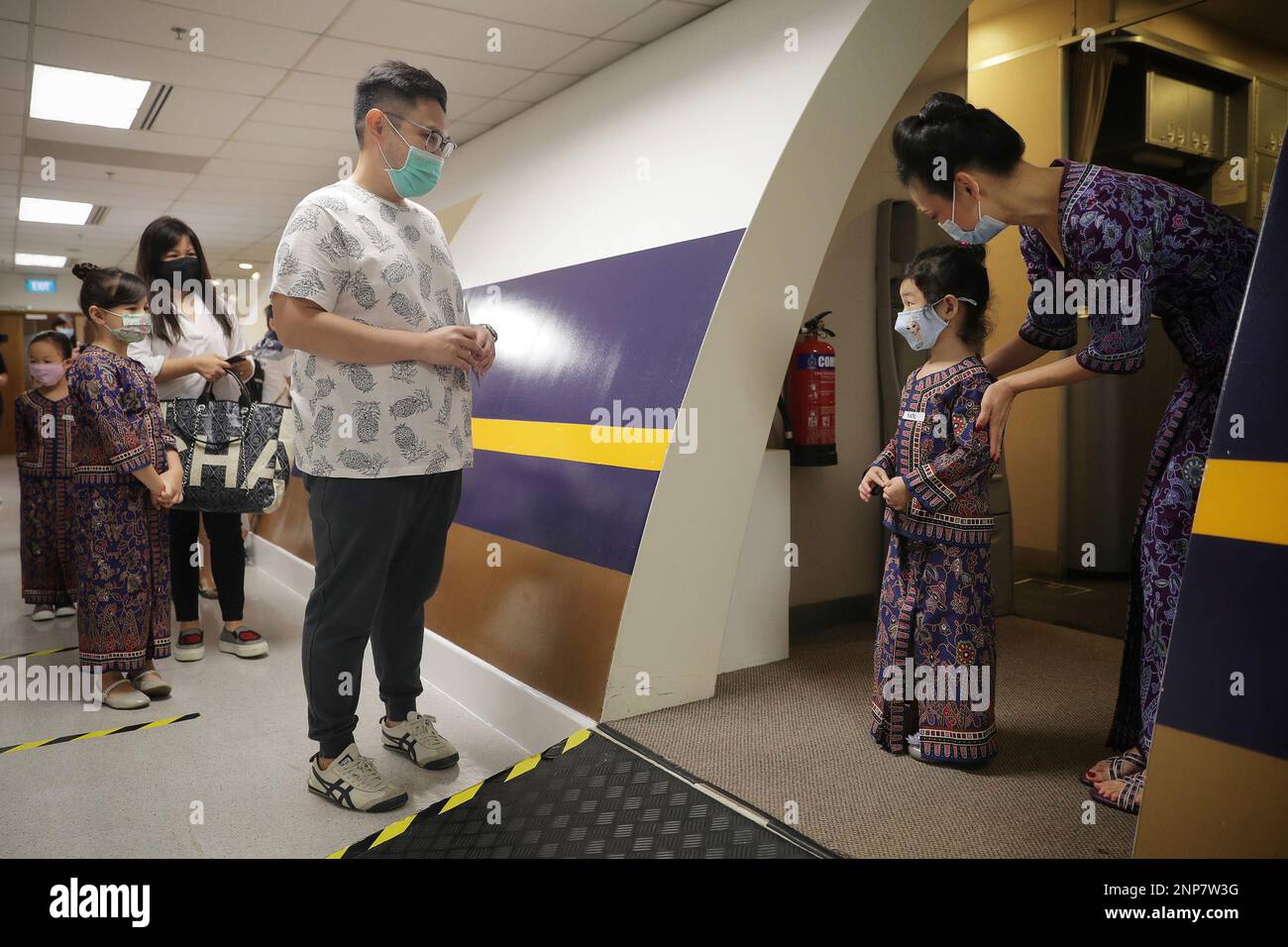 A girl, assisted by an SIA stewardess, greets her father, while taking ...
